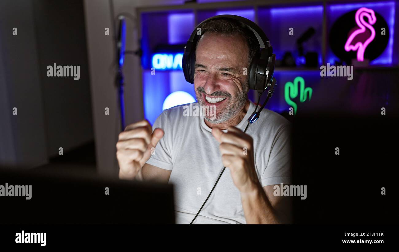 Cheerful middle age man with grey hair ecstatically celebrates his win ...