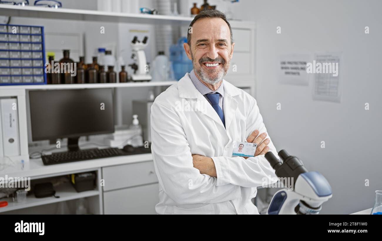 Smiling grey-haired middle-aged scientist man crosses arms, works with ...