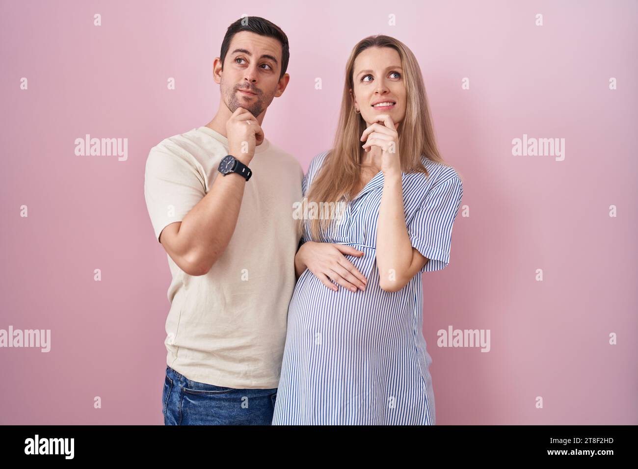 Young couple expecting a baby standing over pink background with hand ...