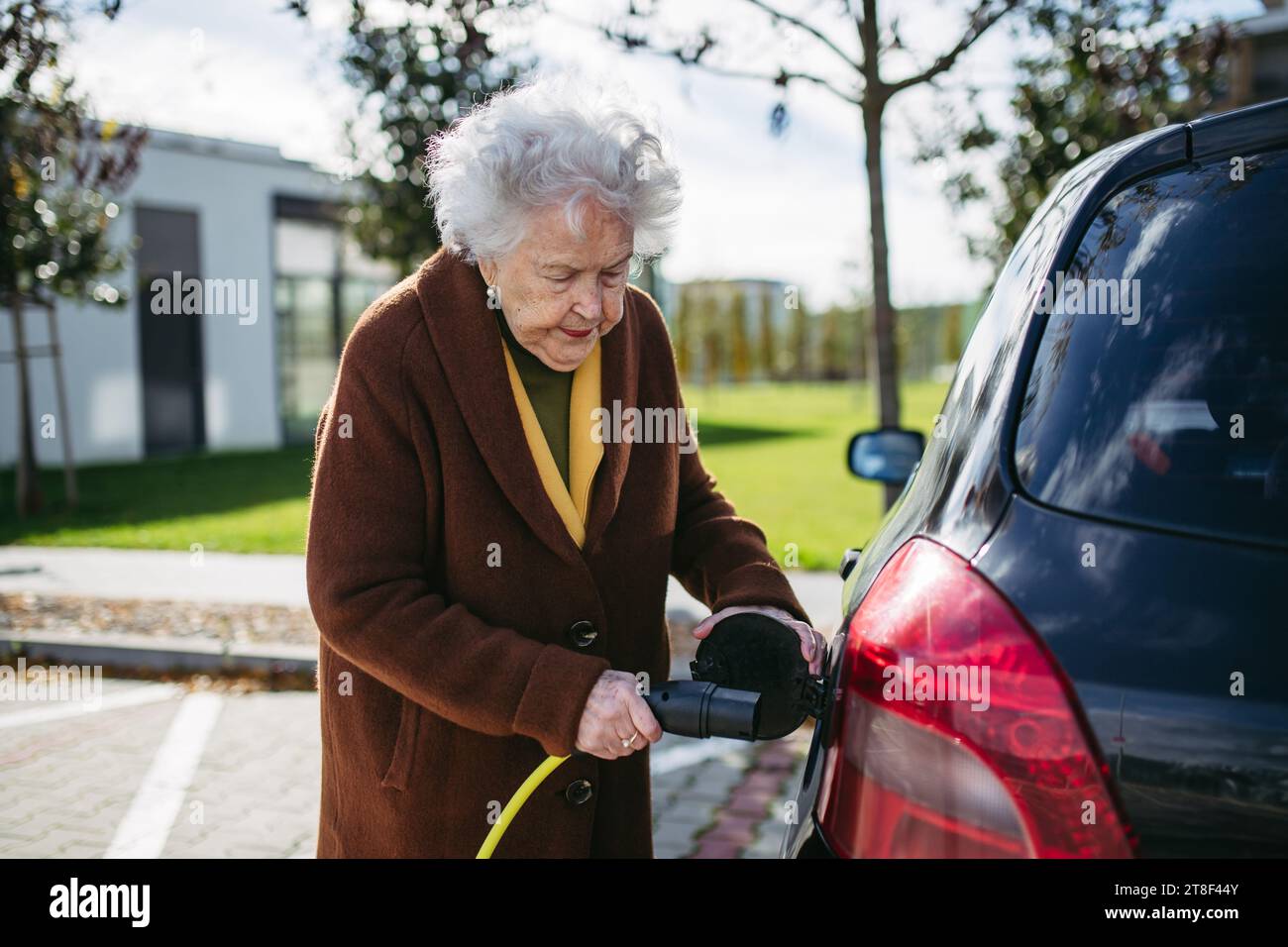 Close up of beautiful senior woman plugging charger in her electric car ...