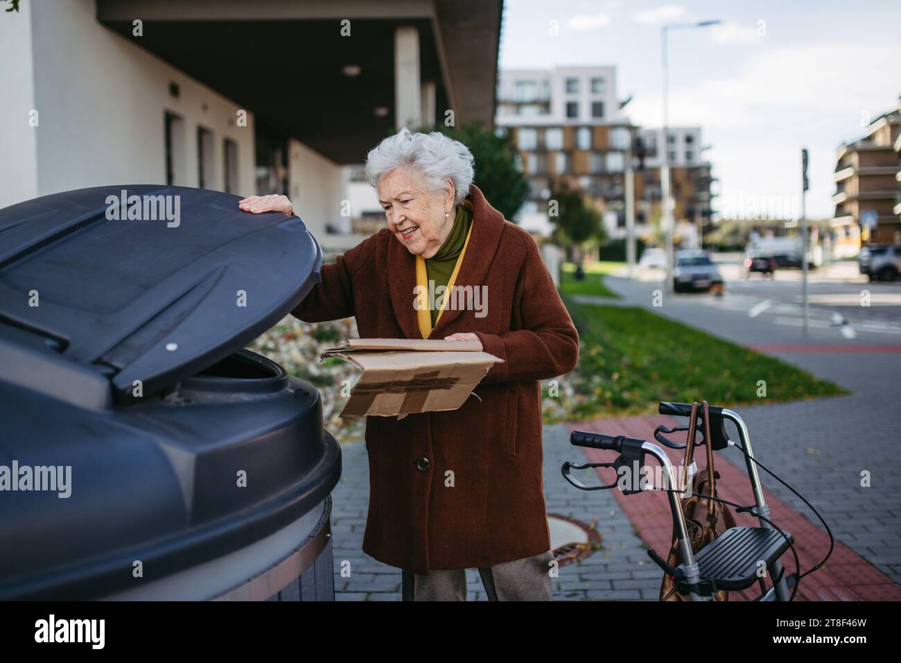 Elderly woman disposing cardboard into the garbage can, waste container ...