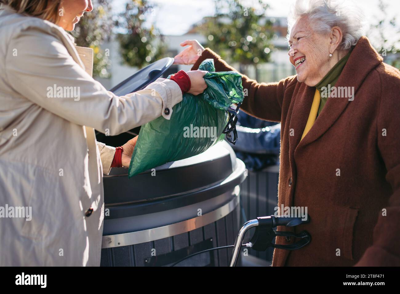 Woman helping elderly neighbor throw away trash into garbage can, waste ...