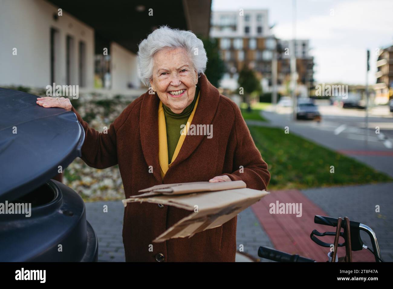 Elderly woman disposing cardboard into the garbage can, waste container ...