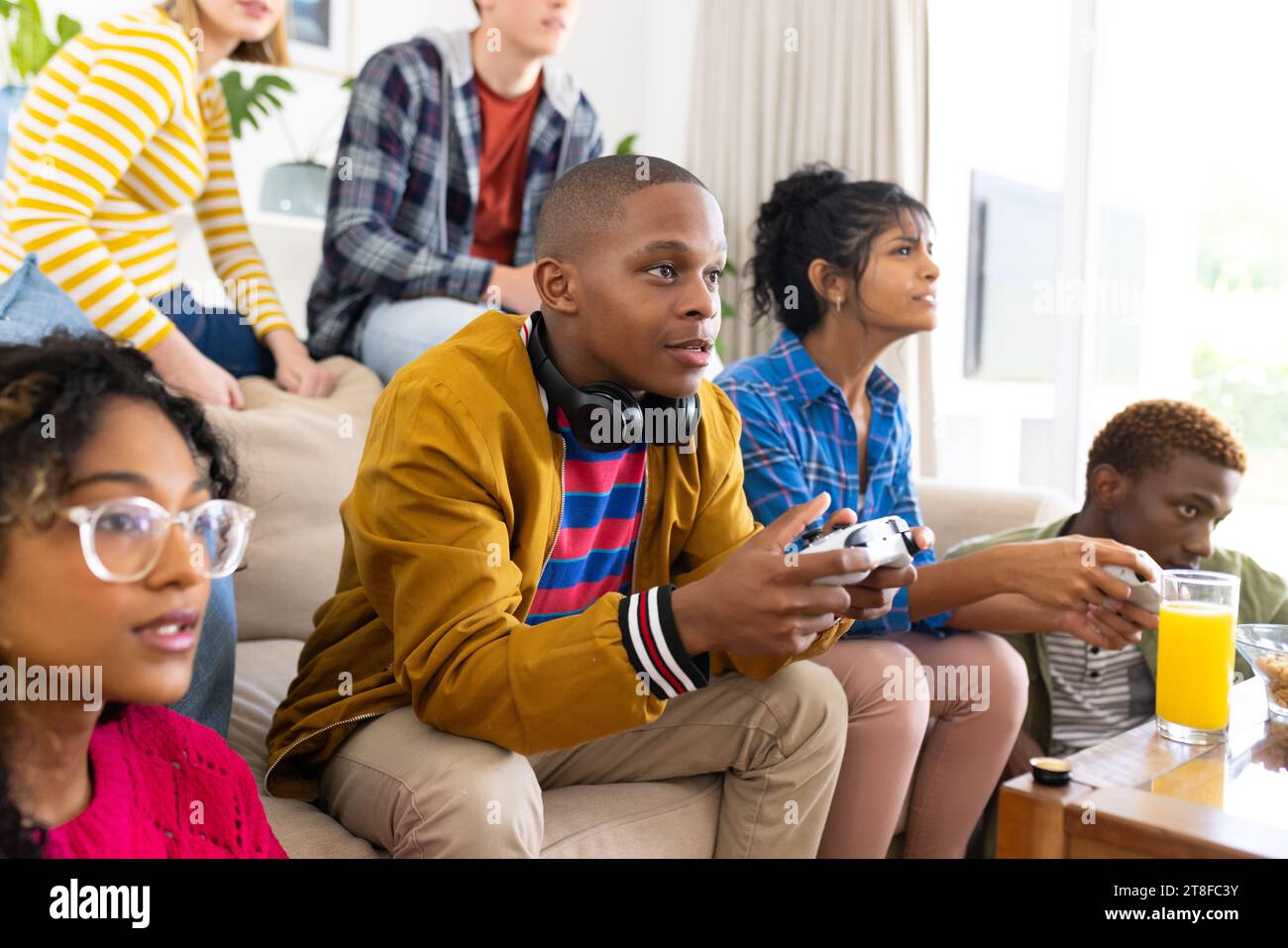 Happy diverse group of teenage friends sitting on couch and playing ...