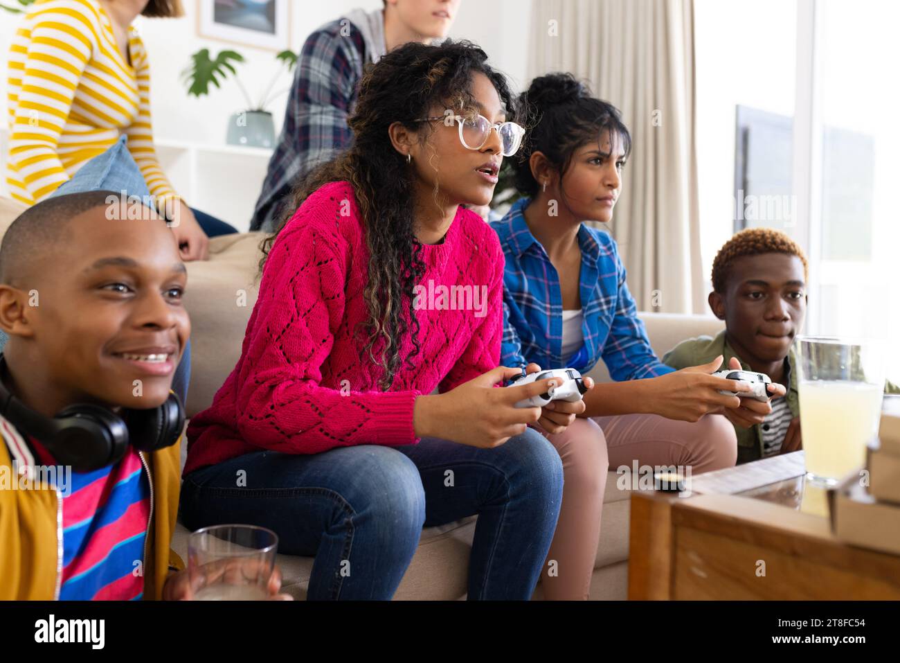 Happy diverse group of teenage friends sitting on couch and playing ...