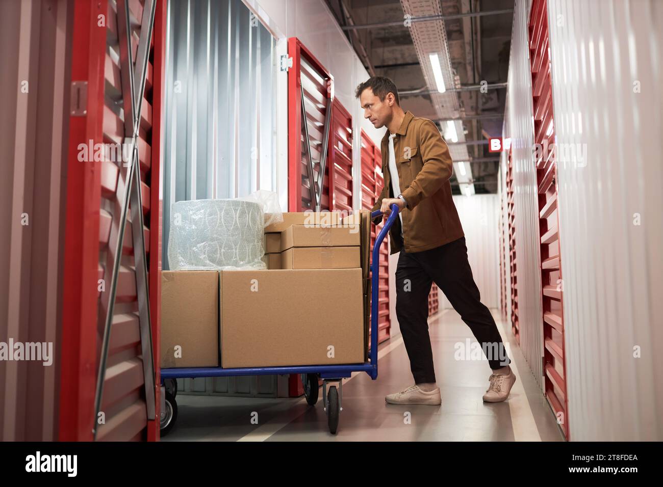 Man pushing cart with boxes inside unit he rents in self-storage ...