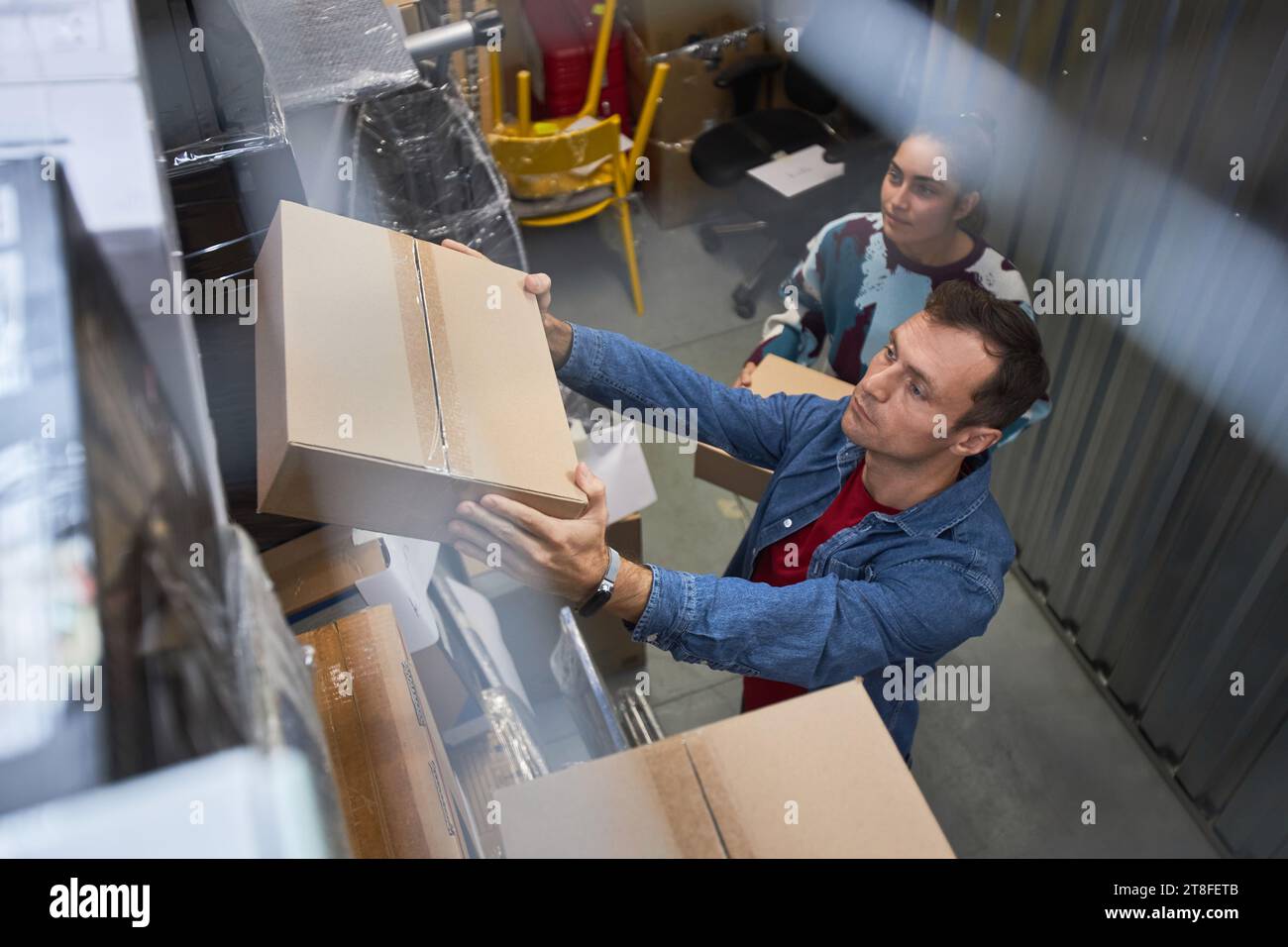 Couple putting packed boxes on shelf in self-storage unit they rent ...
