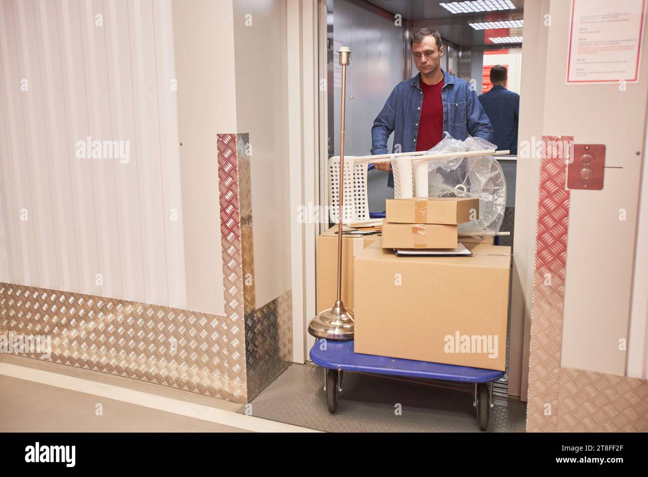 Man pushing cart with furniture and boxes when walking out of elevator ...