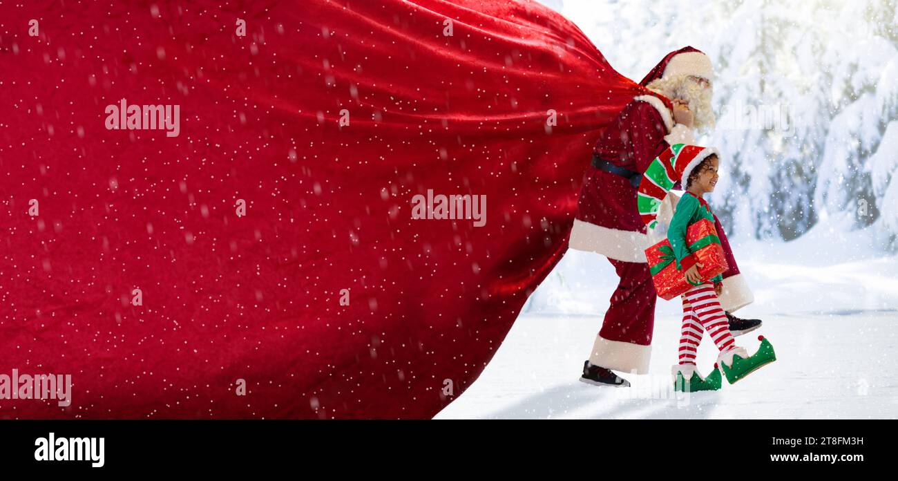 Santa and elf deliver Christmas presents. Santa Claus and little child carry a huge sack with ...