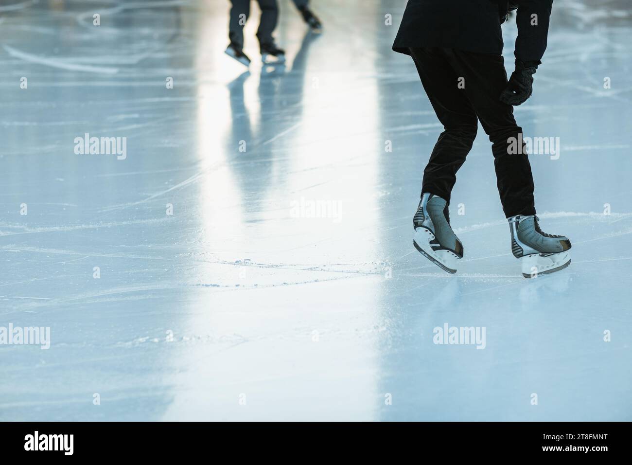 Close-up of ice skater's feet on a shiny outdoor rink, with others in ...
