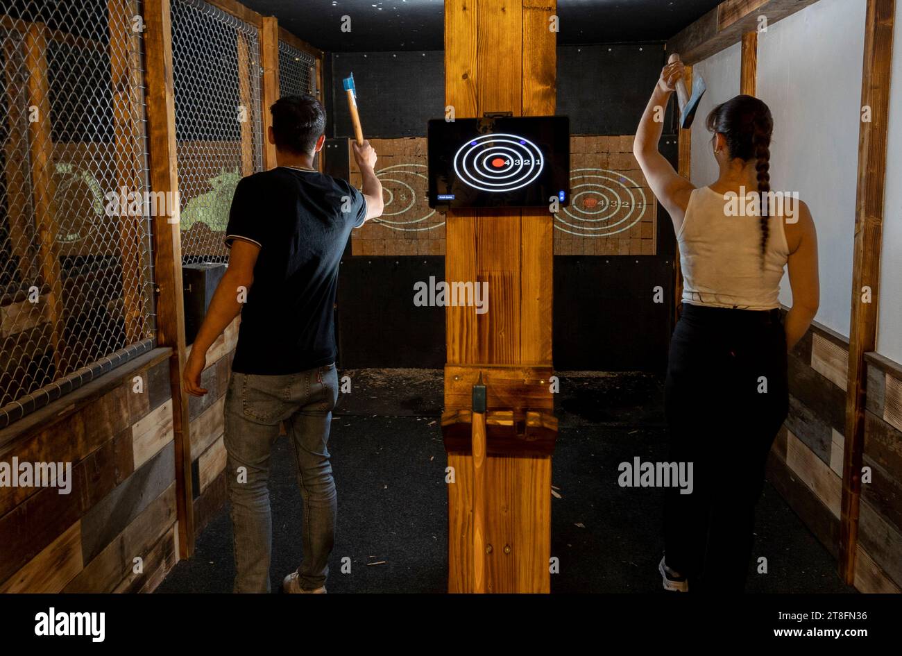 A man and woman participate in an axe throwing activity, aiming at a ...