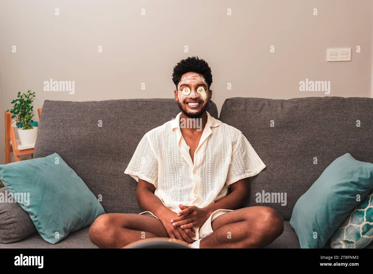 Cheerful latin man enjoying a self-care routine with a facial mask ...