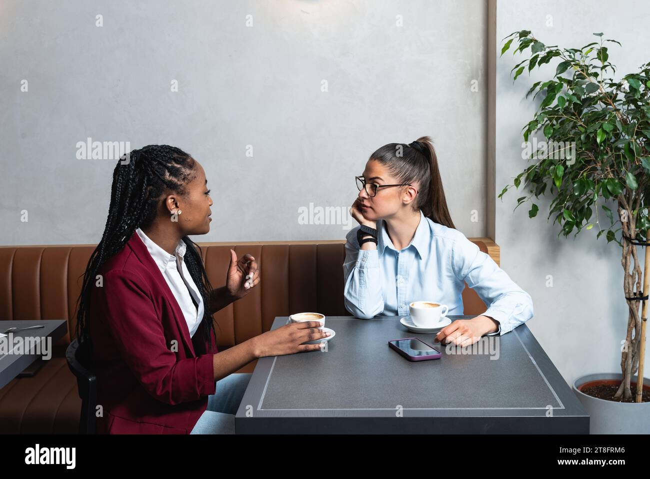 Two young business woman colleagues taking a break in nearby cafeteria ...