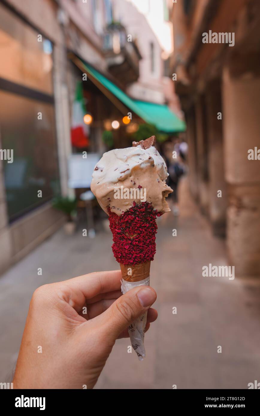 Hand holding ice cream cone in charming narrow street with cozy ...