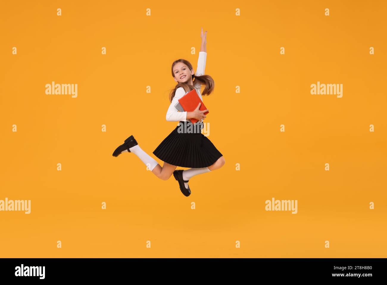 Happy schoolgirl with books jumping on orange background Stock Photo ...