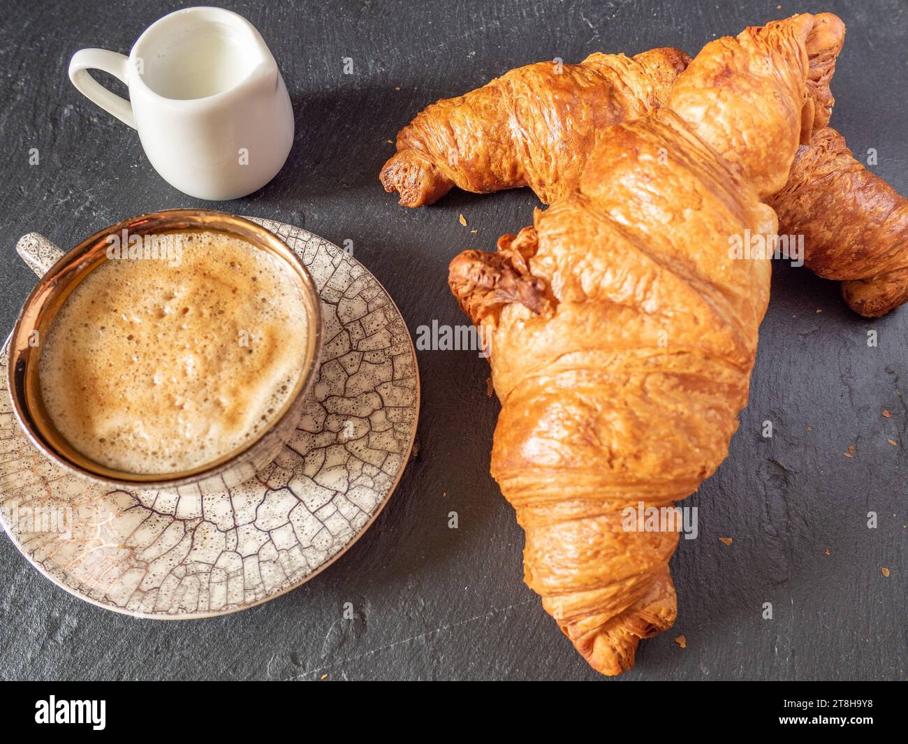 A freshly baked croissant and a cup of steaming hot coffee placed on a ...