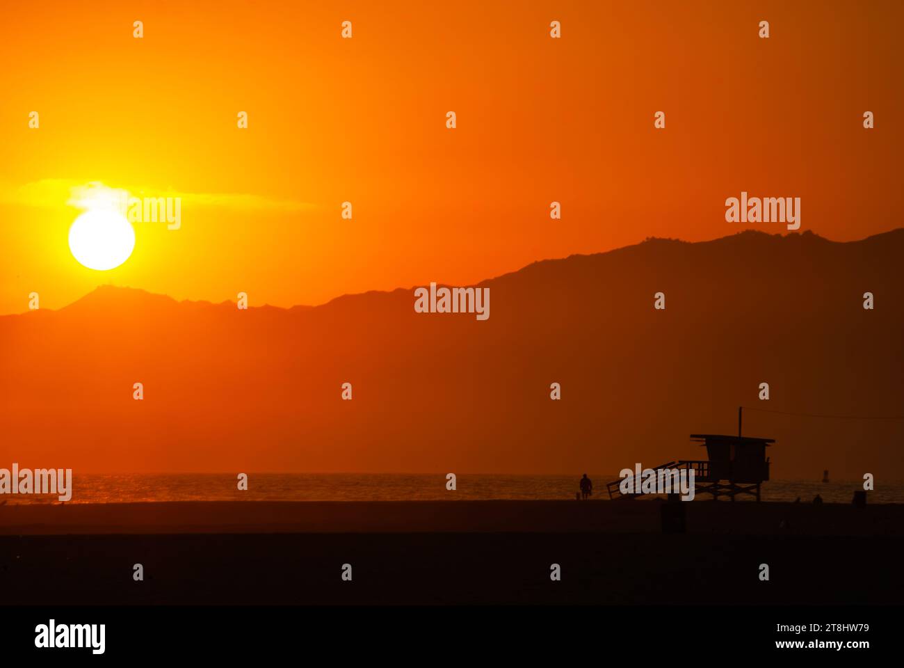 A group of silhouetted figures stand on a beach as the sun sets in the ...