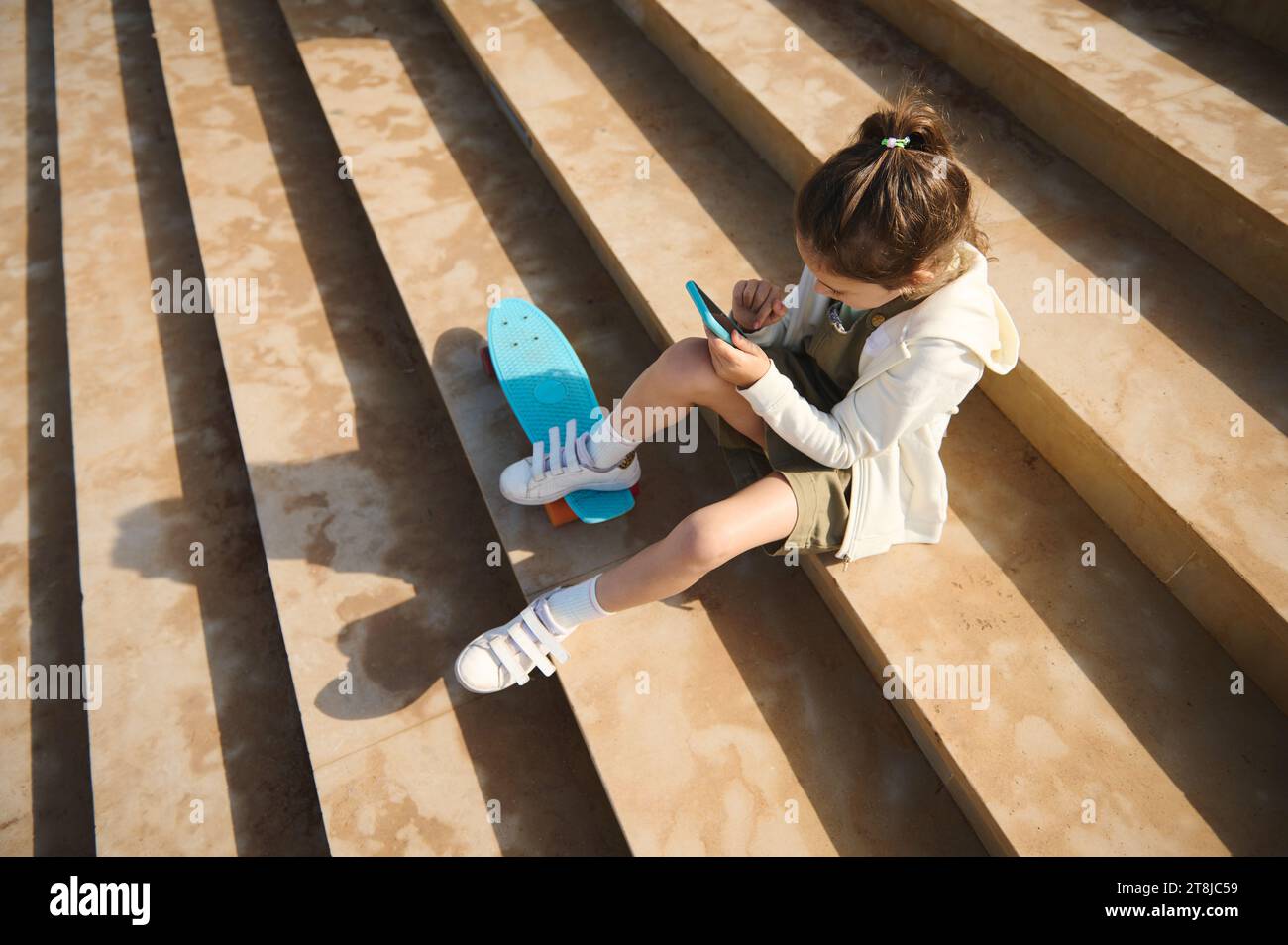 Overhead view of a child girl using modern smartphone sitting on steps ...