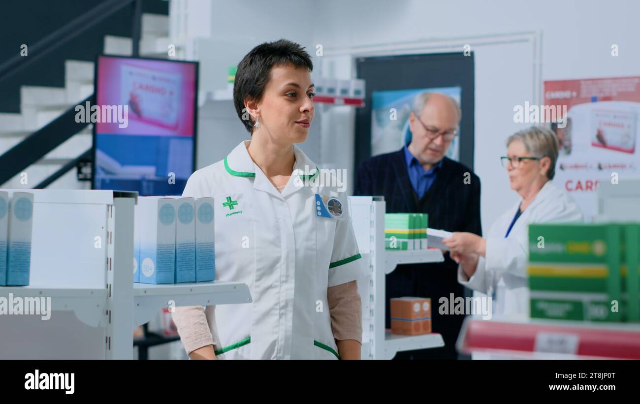 Friendly pharmacist in apothecary placing pills box on shelves while ...