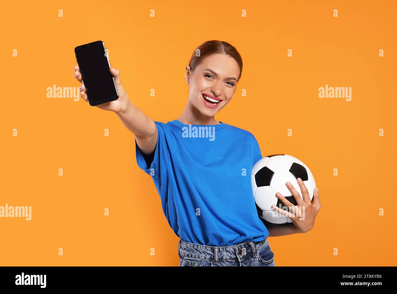 Happy fan with football ball showing smartphone on orange background ...