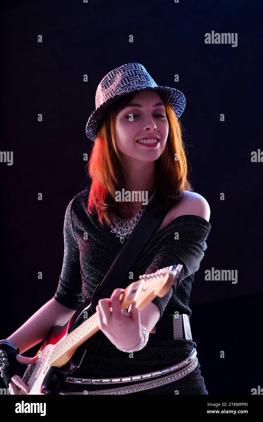 Radiant female guitarist with red hair strums her instrument with ...