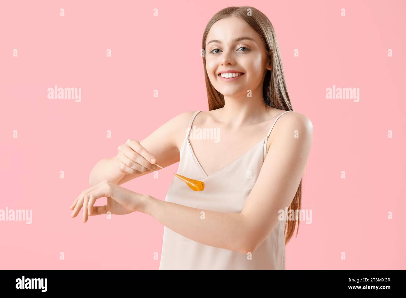 Young woman applying sugaring paste onto her arm against pink ...