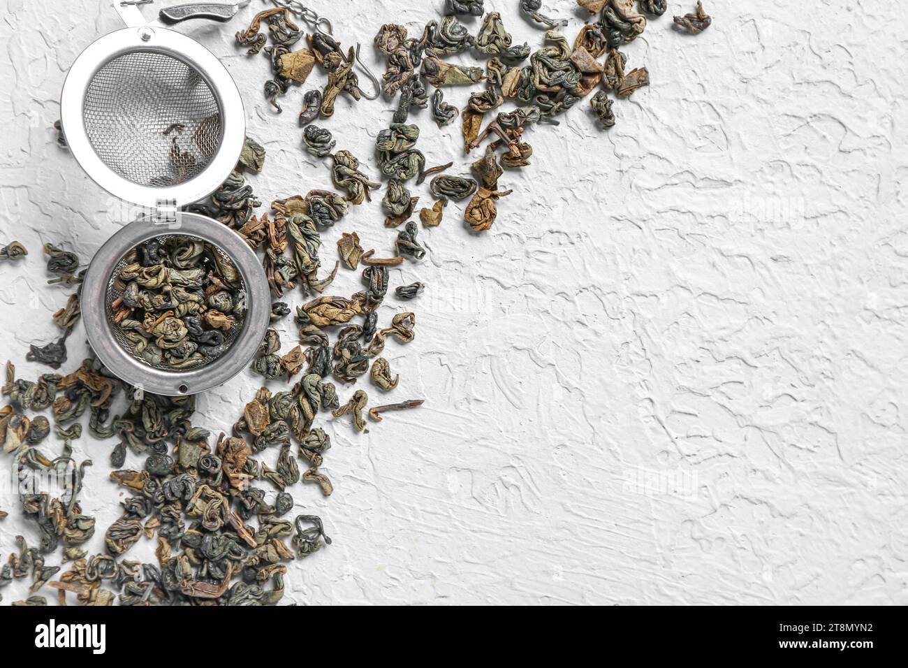 Metal infuser with green tea leaves on white textured background Stock ...