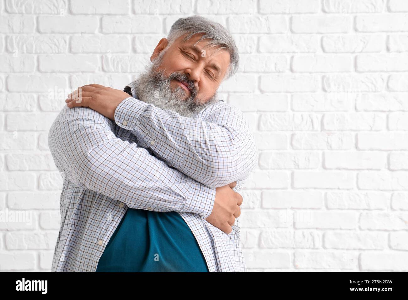Mature man hugging himself on white brick background Stock Photo - Alamy