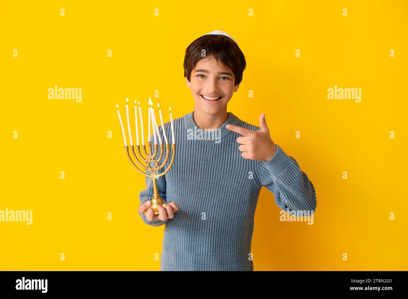Little Israeli boy in kipa pointing at menorah on yellow background ...