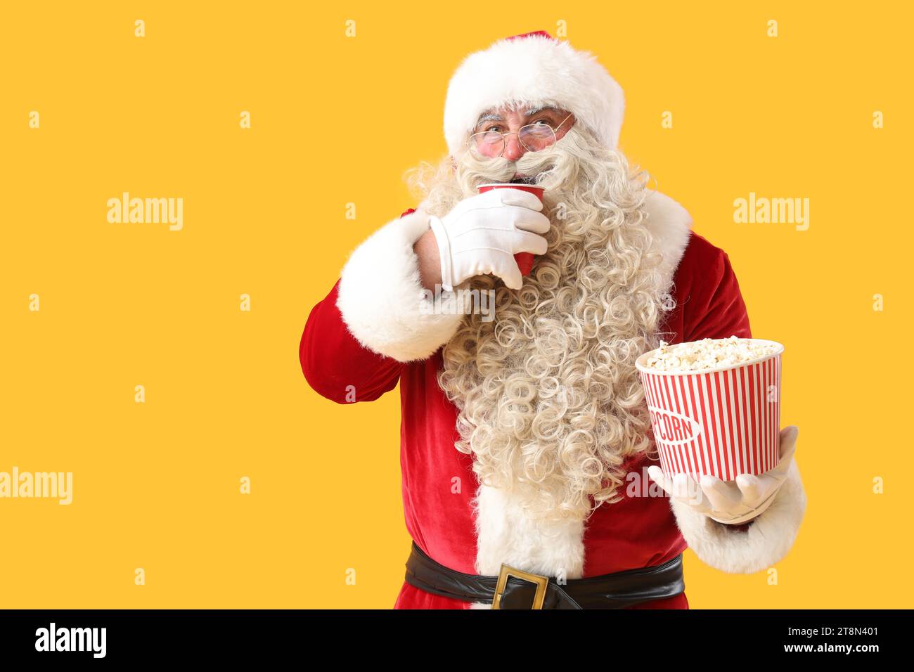 Santa Claus with cup of cola and tasty popcorn on yellow background ...
