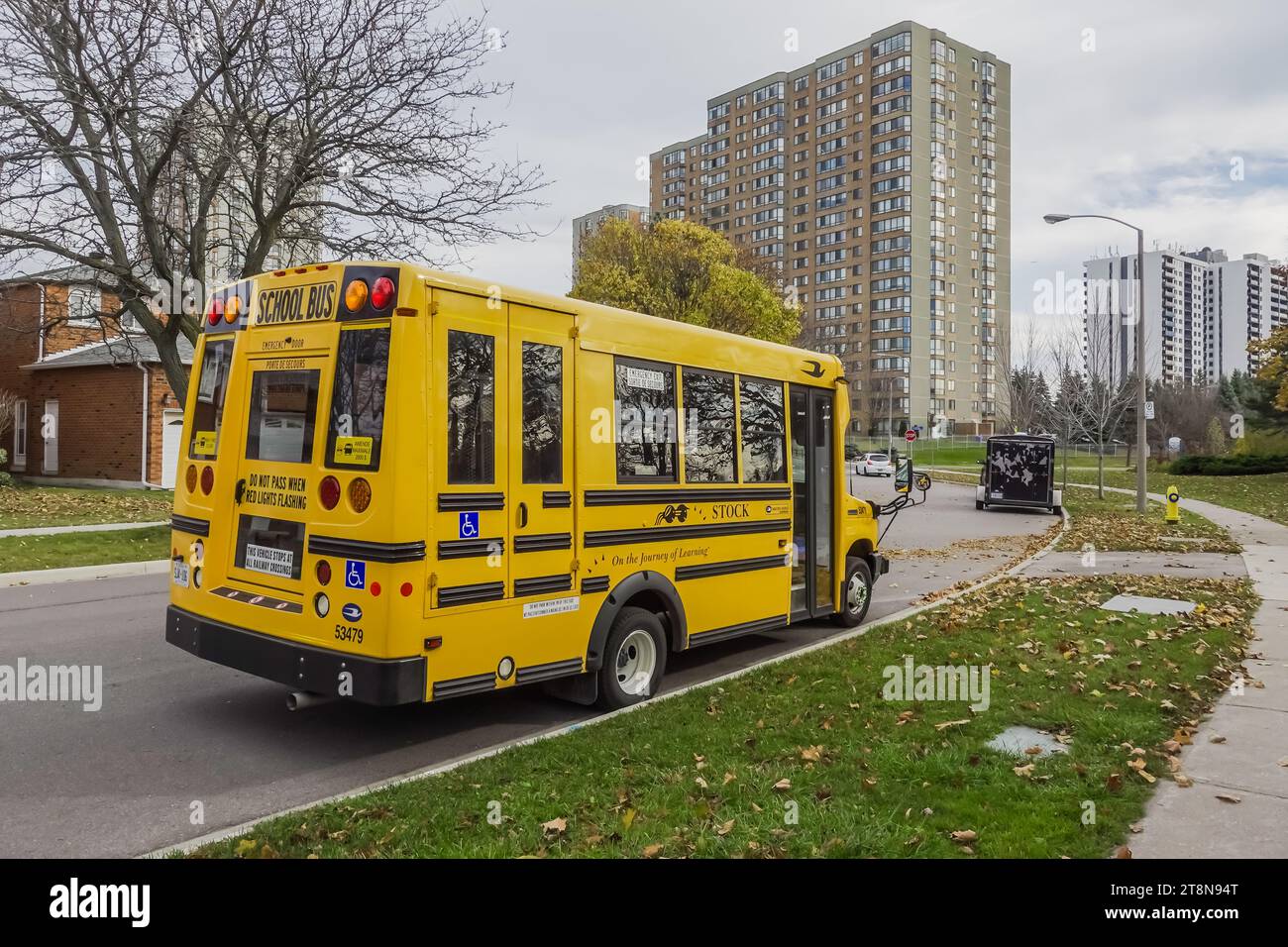 A yellow school bus parked on the side of a road with apartment ...
