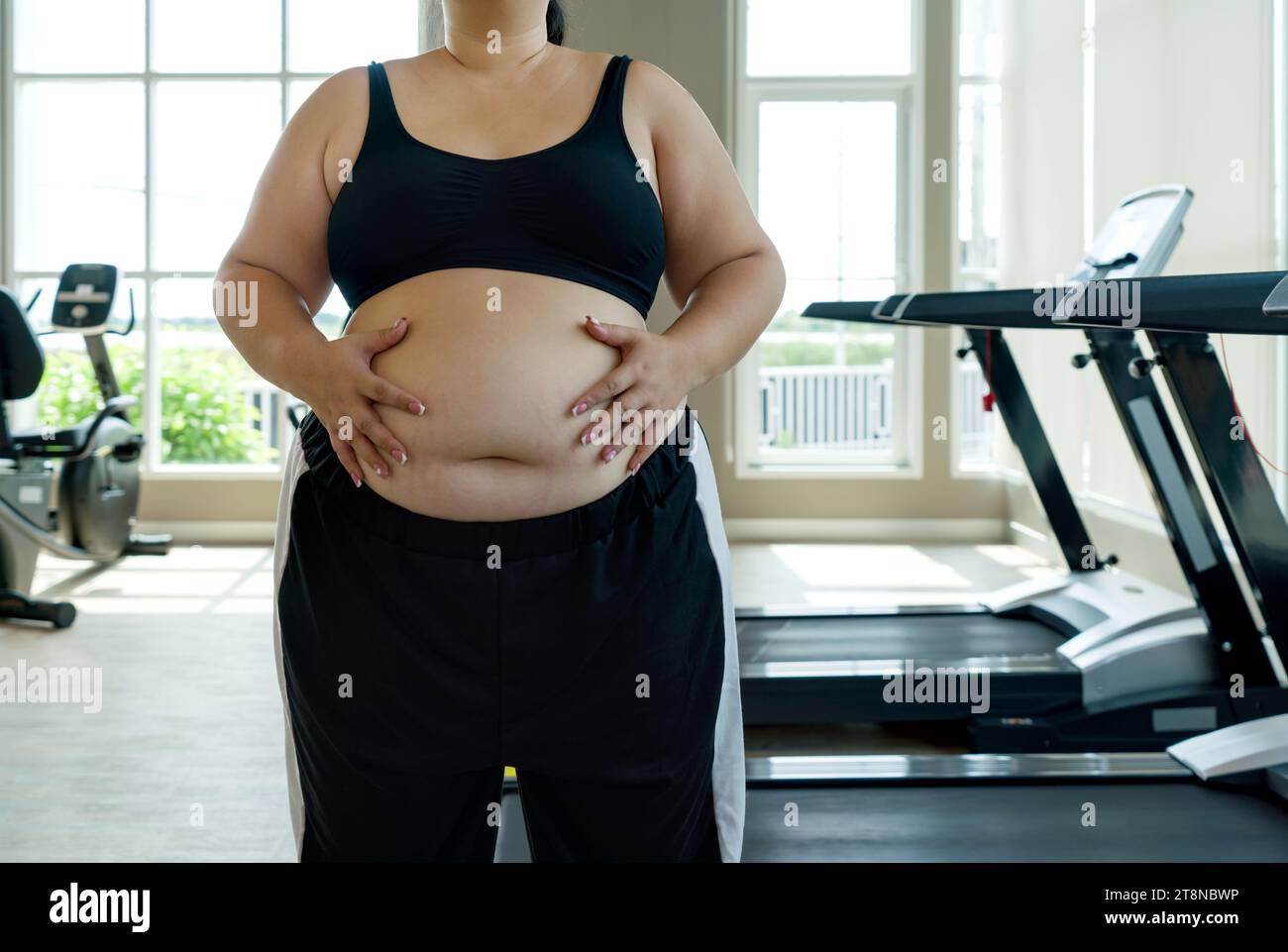 A plus-sized woman placing her hand on her belly, standing confidently ...