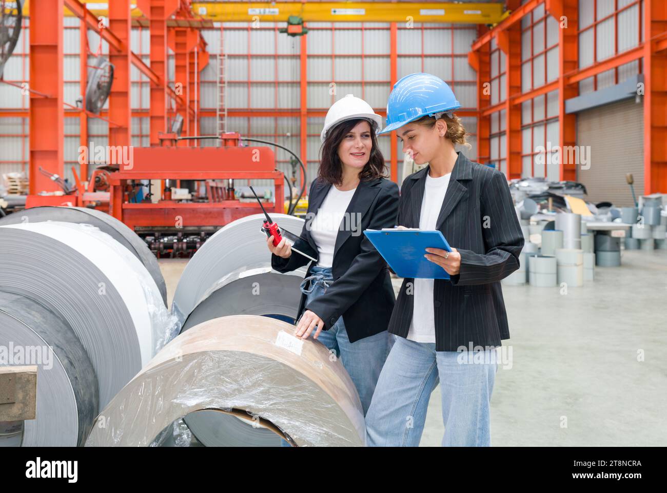 Two ladies with safety helmet are observing metal roll inside an ...