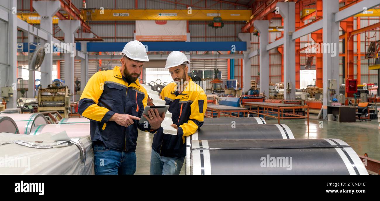 Two factory workers are inspecting a stack of large steel coils in an ...