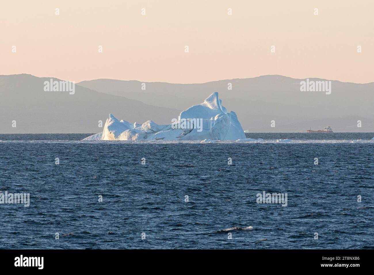An iceberg floats in the rising morning sun against the silhouette of ...