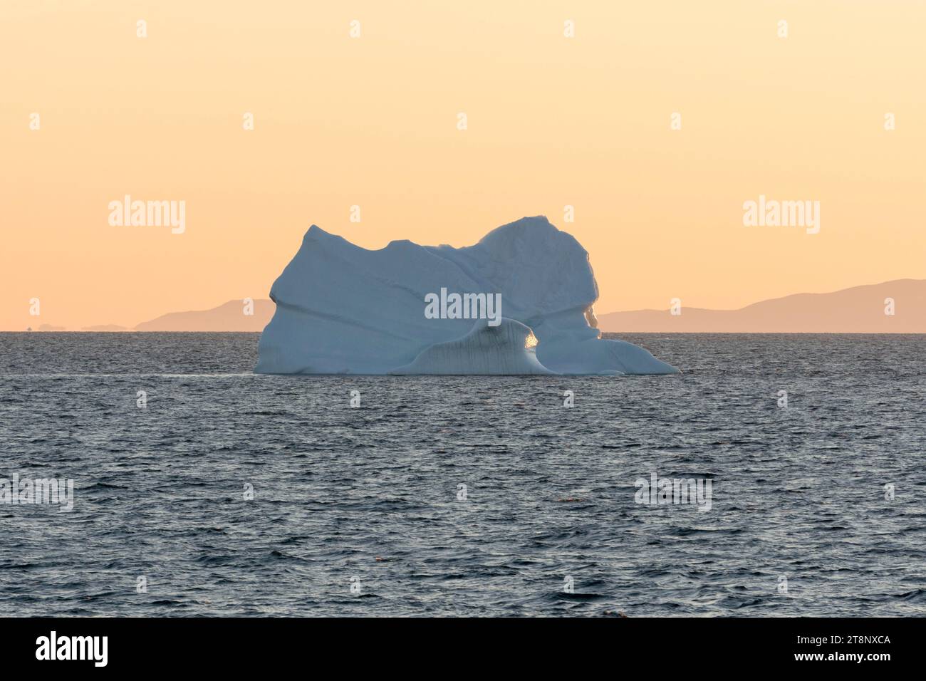 An iceberg floats in the rising morning sun off the mountains of the ...