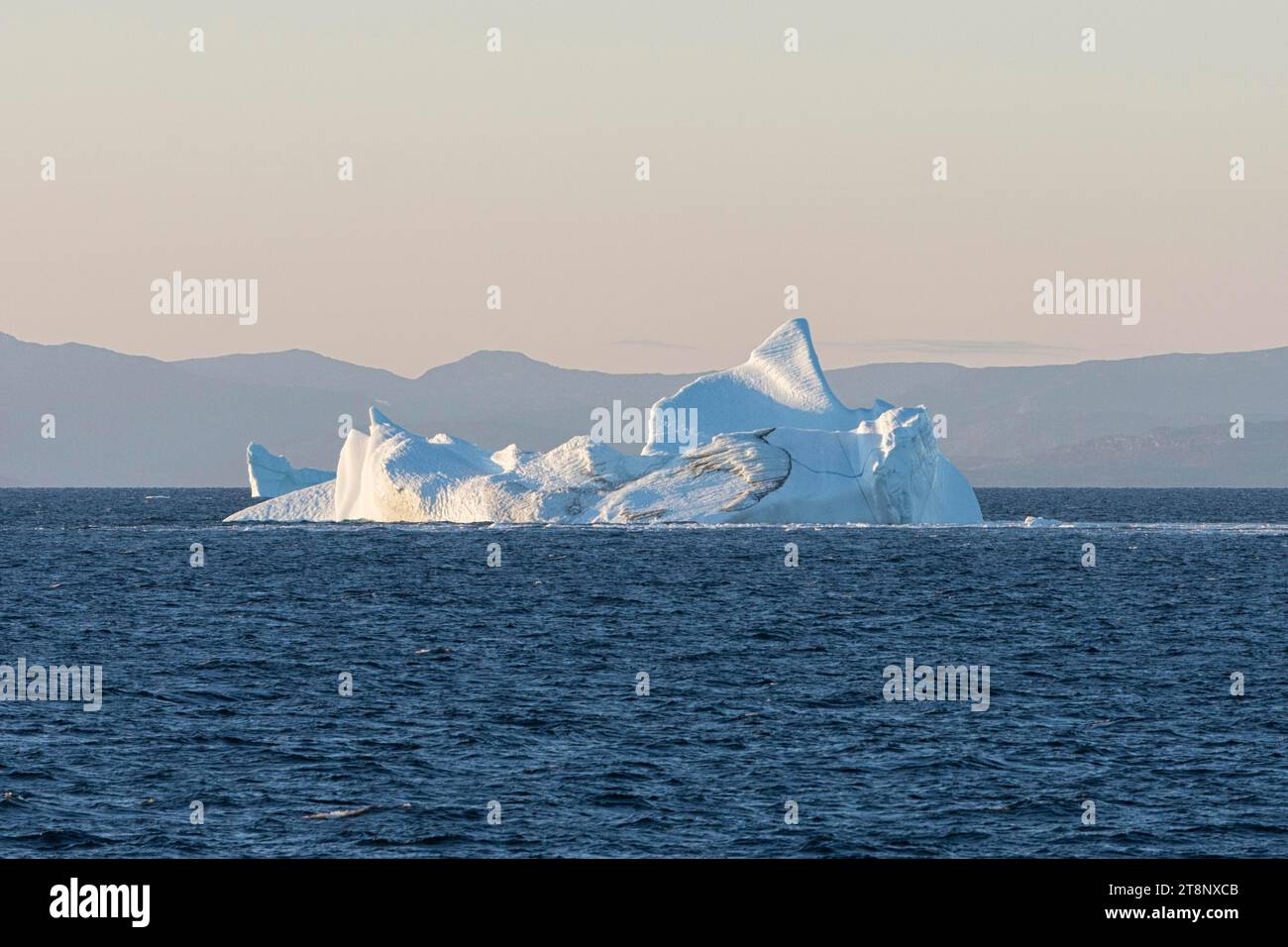 An iceberg floats in the rising morning sun off the mountains of the ...