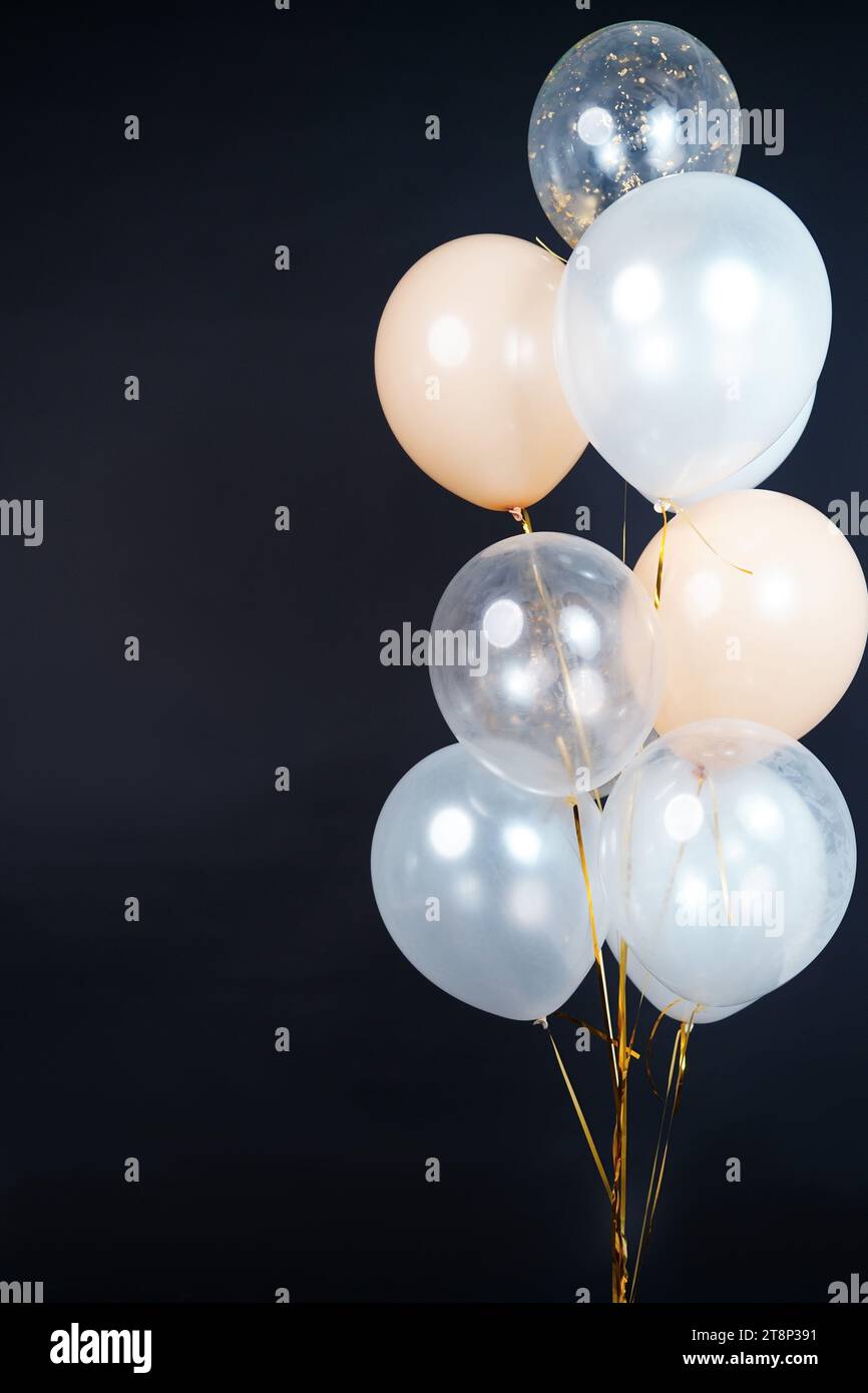 A bunch of balloons in white, beige and transparent colors on a dark ...
