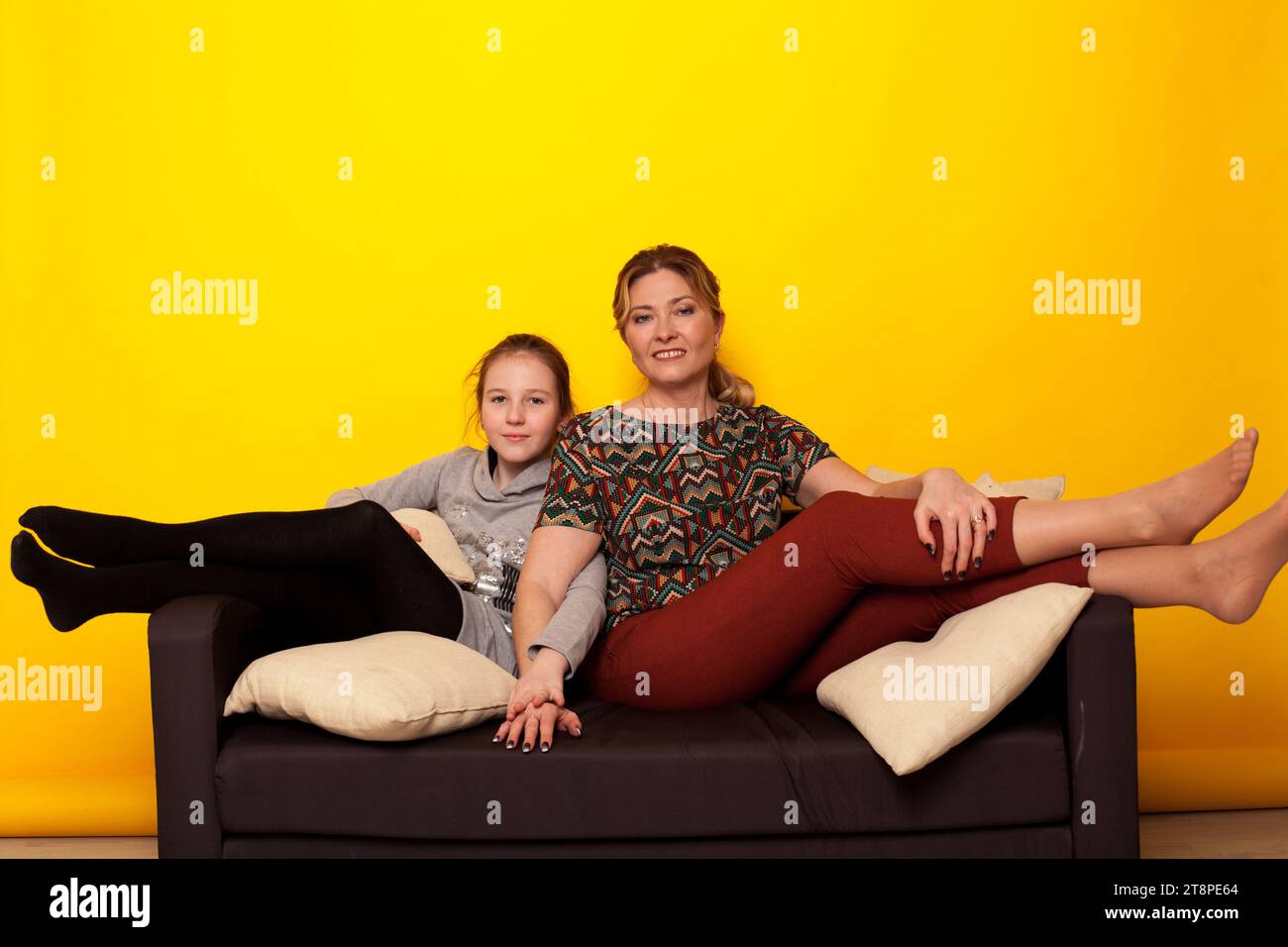 mother and daughter family sitting on the couch on a yellow background ...