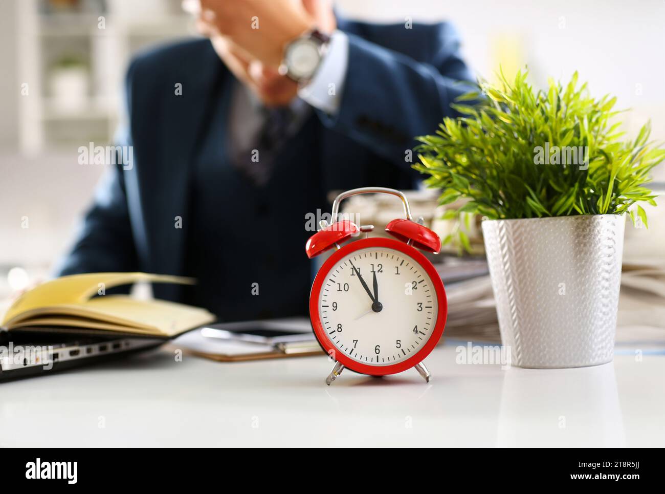 Red alarm clock shows late time closeup and tired office male clerk in ...