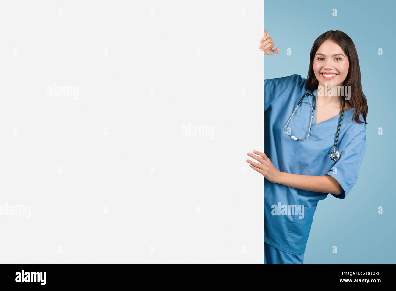 Young European nurse in blue coat peeking from placard Stock Photo - Alamy