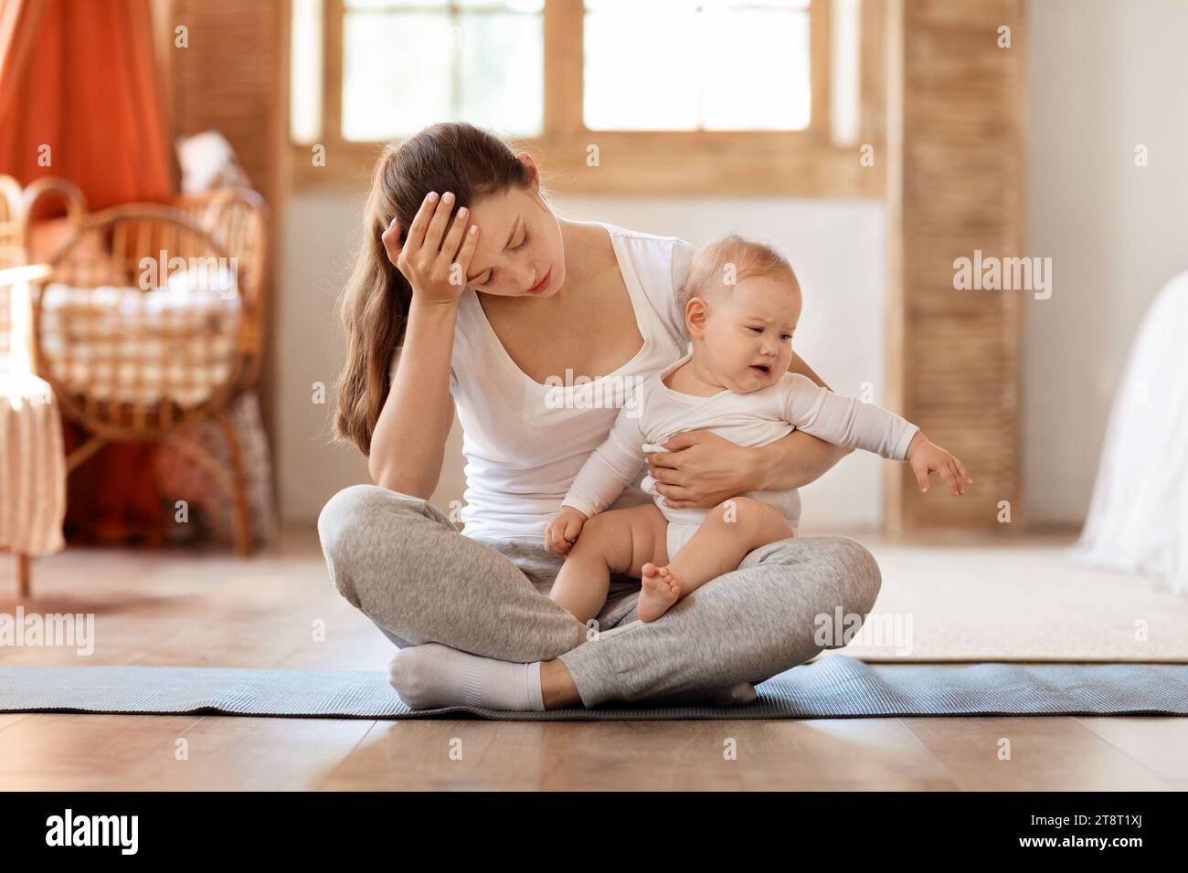 Exhausted mother sitting on fitness mat with crying little baby Stock ...