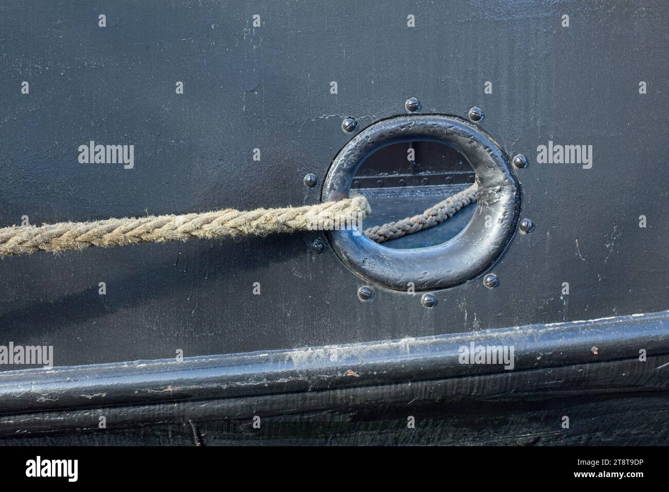 Closeup of a thick twisted mooring rope comig out of hole in the side ...