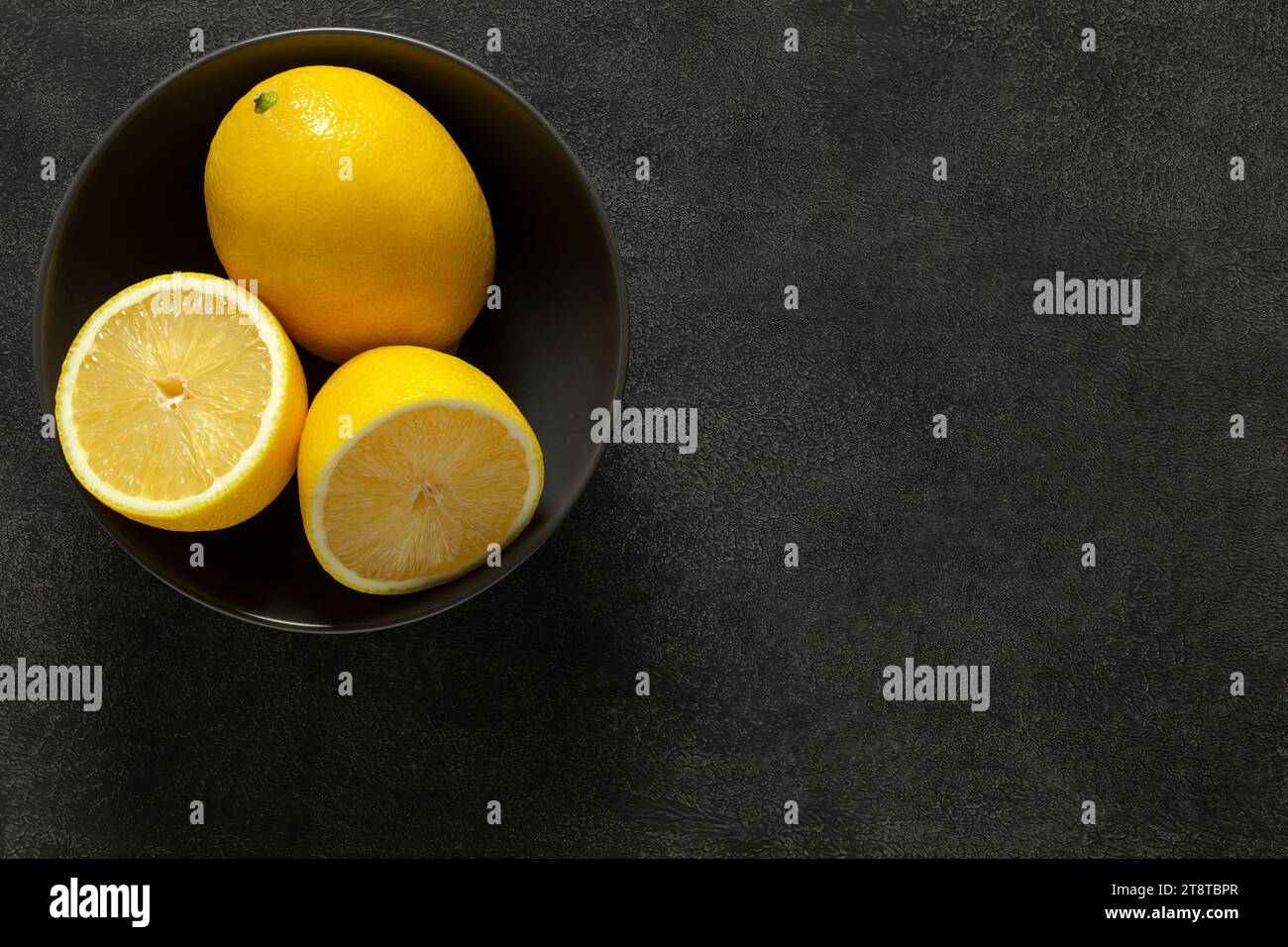 Lemons whole and cut in grey bowl, on dark background, top view, space ...