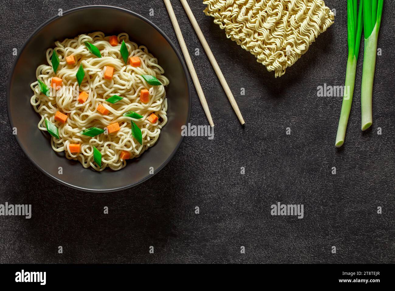 Instant noodles, cooked in vegetables and green onions, on dark ...