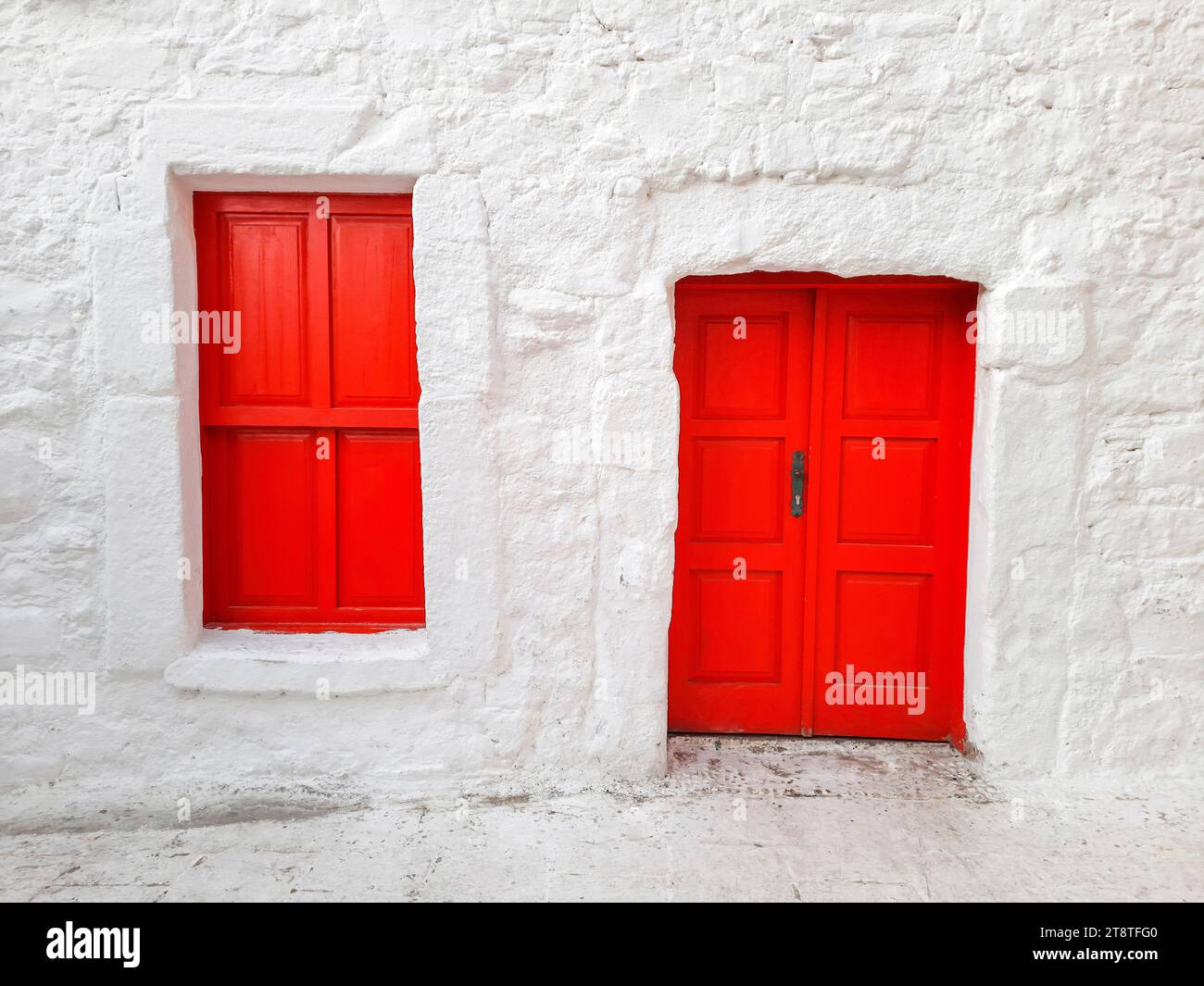 Door and window with closed shutters of red color in a house with white ...