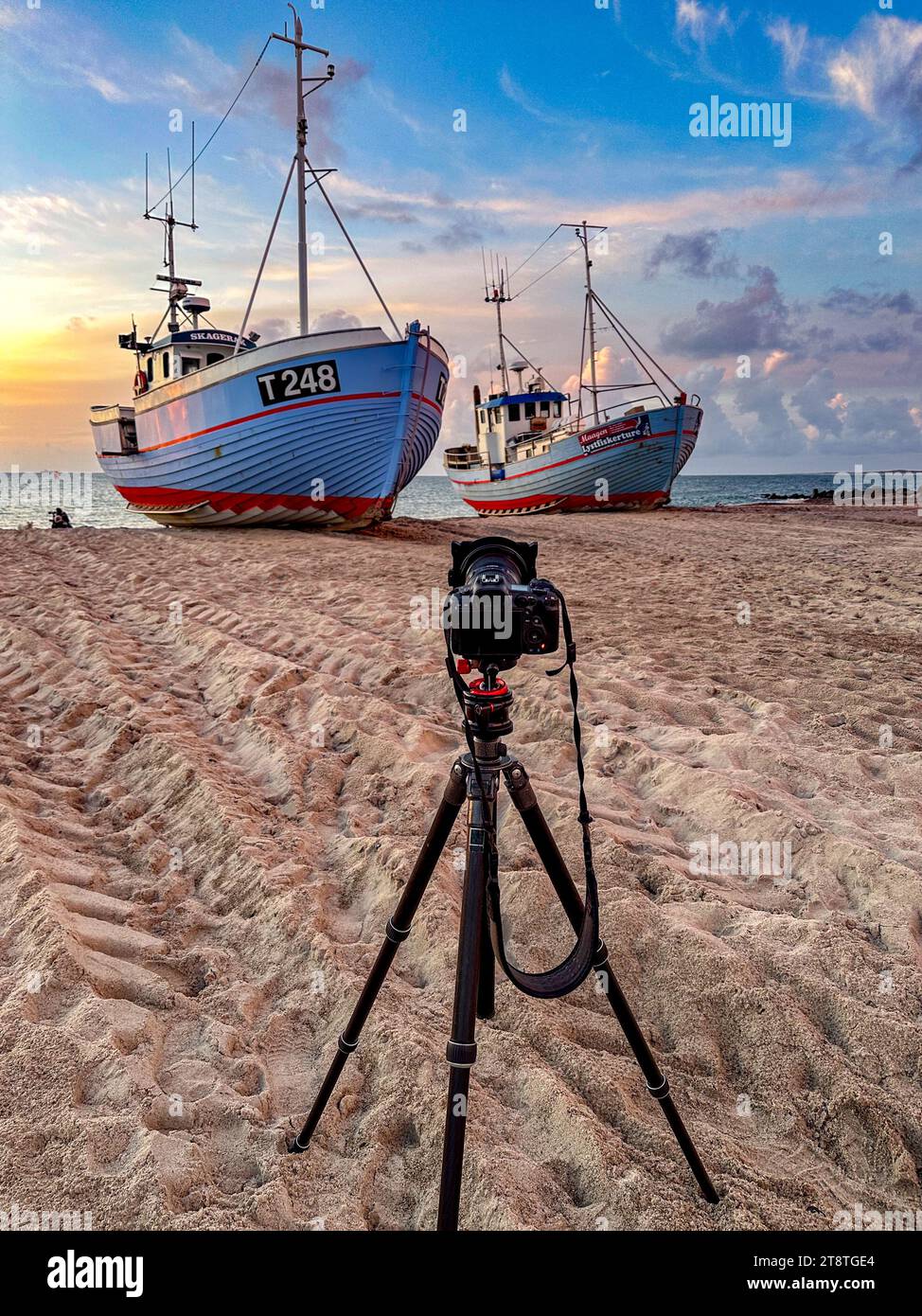 Camera on tripod photographing fishing boats on the beach at sunset in ...