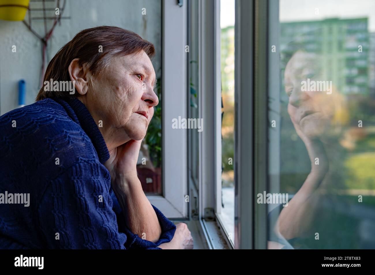 Portrait of a sad elderly woman looking out the window at home. A ...