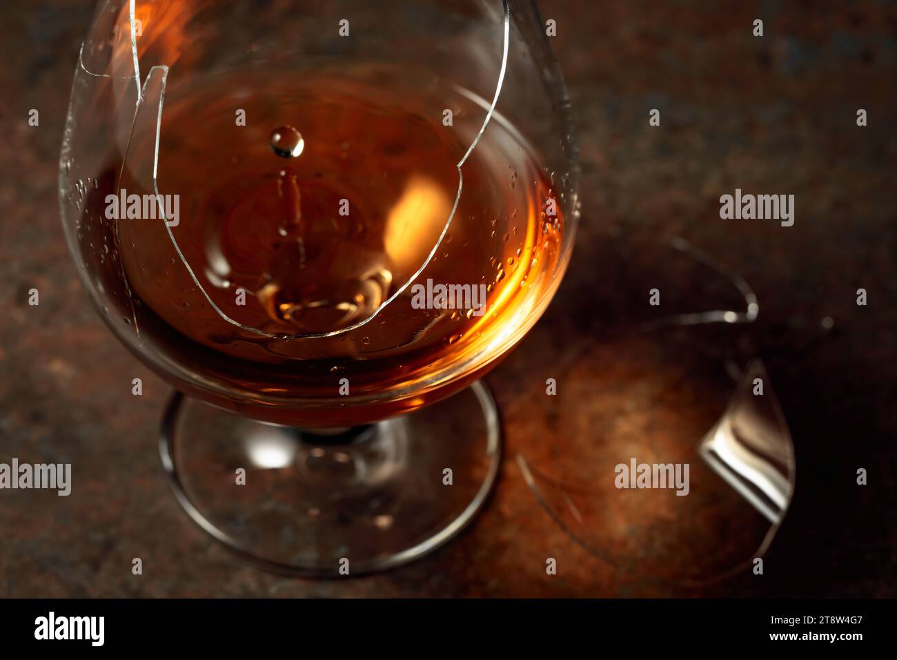 Brandy is in a broken glass on a rusty background. The drop of drink ...
