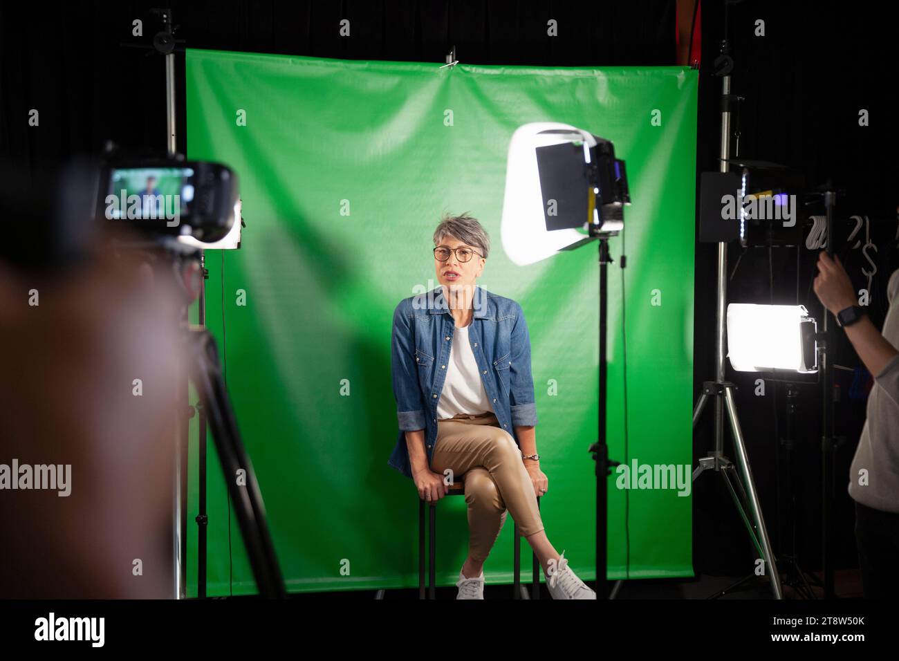 Mid adult woman giving an interview while sitting against green screen ...